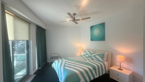 Quarto de hotel com cama, ventoinha no teto, mesa de cabeceira, luminária e janela com cortinas.
