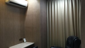 Quarto com escrivaninha, duas cadeiras, uma poltrona de couro preto, ar condicionado e cortina.