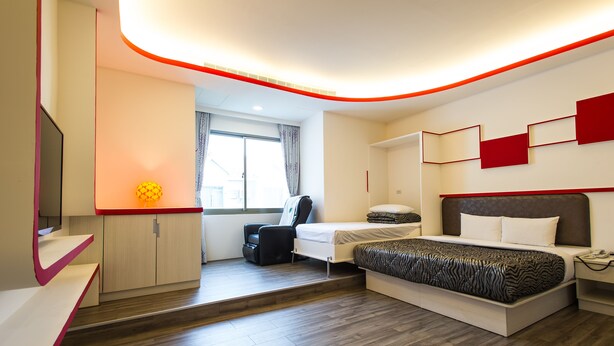 Quarto de hotel moderno com cama, mesa de cabeceira, poltrona e escrivaninha com cadeira.