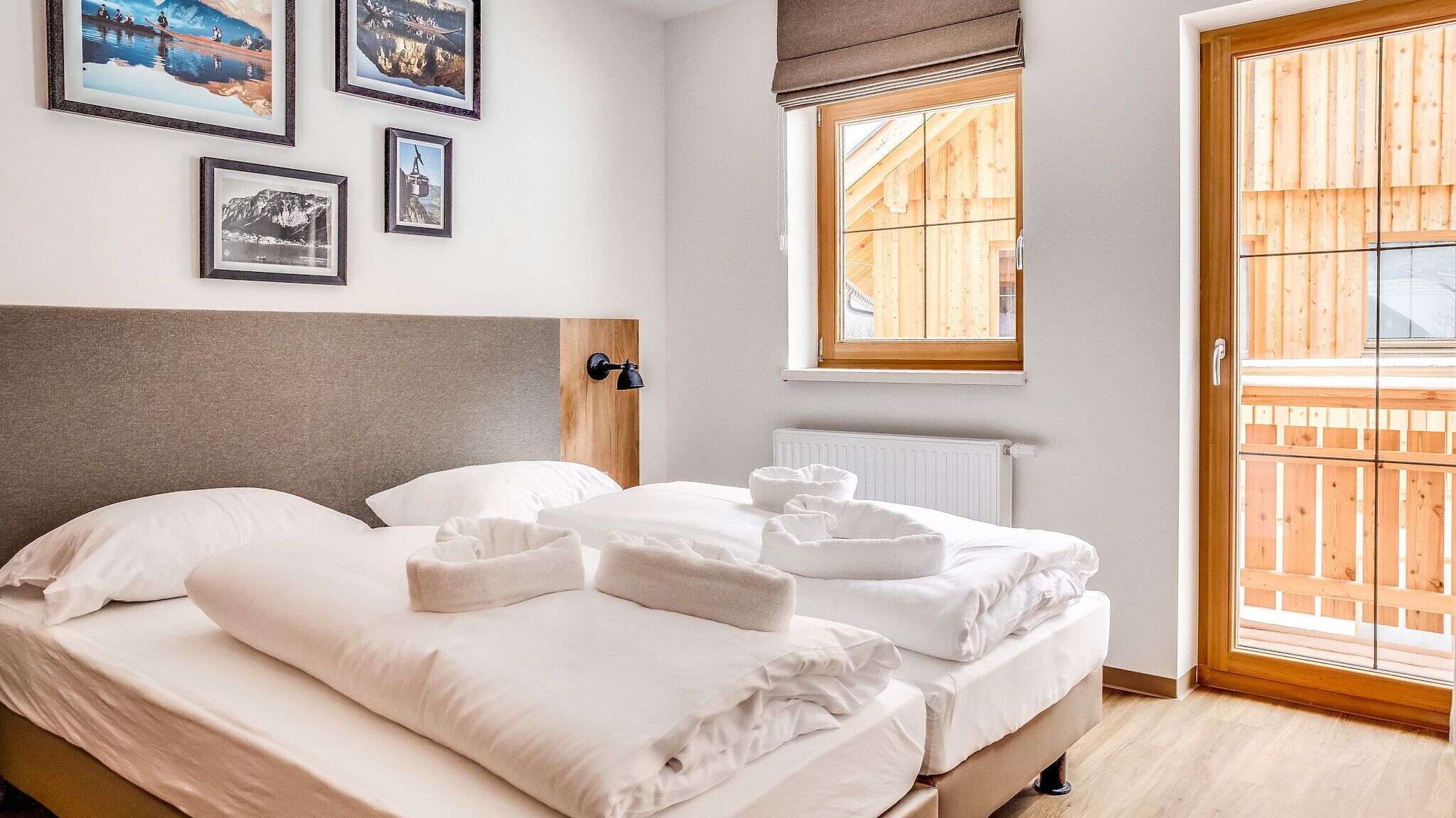 Quarto com uma cama grande, cabeceira de madeira, janela com vista para um deck de madeira e quadros na parede.