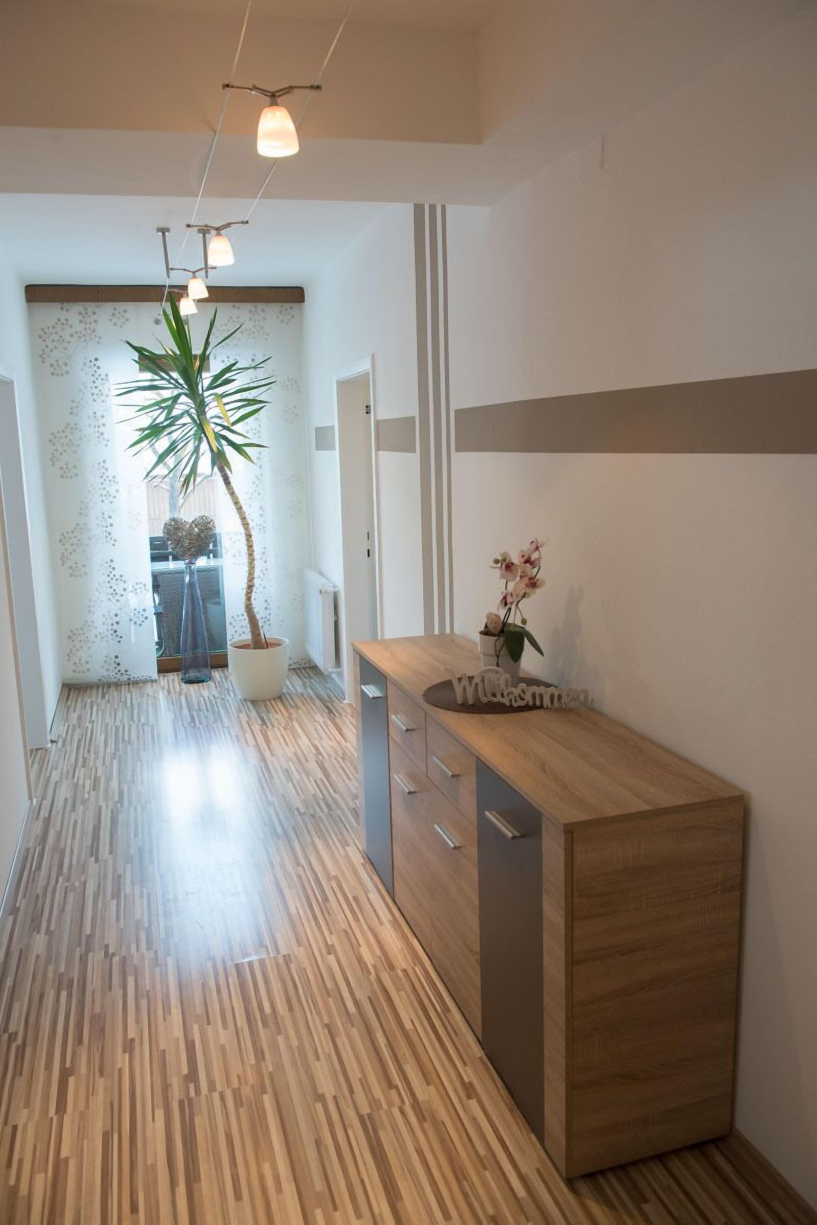 Um corredor com piso de madeira, balcão de recepção, uma planta em vaso e uma parede com painel decorativo.
