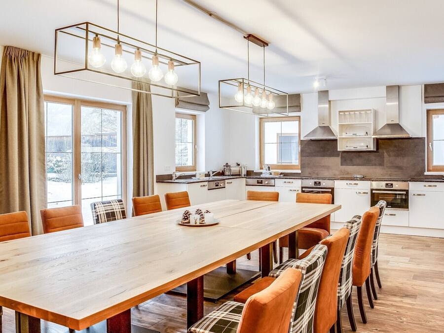 Cozinha moderna com mesa de jantar de madeira, armários brancos e iluminação pendente.
