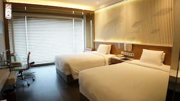 Quarto de hotel com duas camas, uma escrivaninha e uma janela grande com persianas.