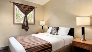 Quarto de hotel com uma cama grande, duas luminárias de cabeceira, uma janela com cortinas e uma mesinha de cabeceira.