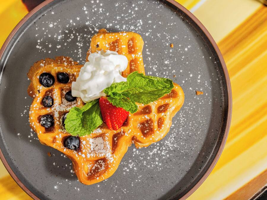 Um waffle em formato de coração com amoras, chantilly e uma folha de hortelã em um prato.
