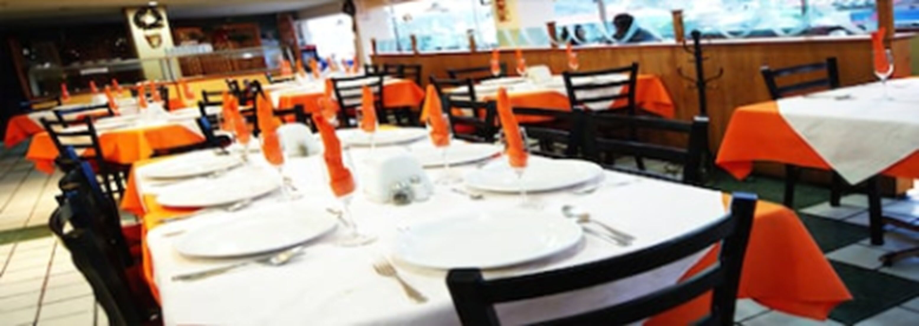 Restaurante com mesas postas para refeição, com toalhas de mesa laranja e pratos brancos.