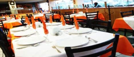 Restaurante com mesas postas para refeição, com toalhas de mesa laranja e pratos brancos.