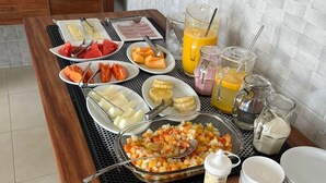 Um buffet de café da manhã com diversas frutas, legumes e bebidas sobre uma mesa de madeira.
