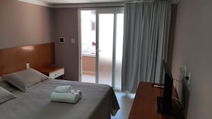 Quarto de hotel com uma cama, uma escrivaninha, uma televisão e uma porta de correr para uma varanda.