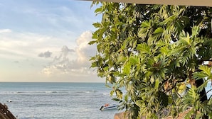 Uma rede numa varanda com vista para uma praia, onde se vê o mar e uma palmeira.