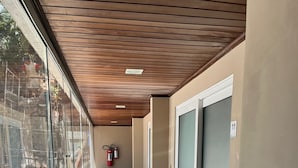 Um corredor com piso de azulejos, teto de madeira e portas de vidro à direita.