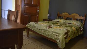 Um quarto com cama de madeira, mesa de cabeceira de madeira, um criado-mudo e uma cadeira.