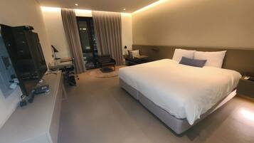 Quarto de hotel moderno com uma cama grande, uma escrivaninha, uma cadeira e vista para a cidade pela janela.
