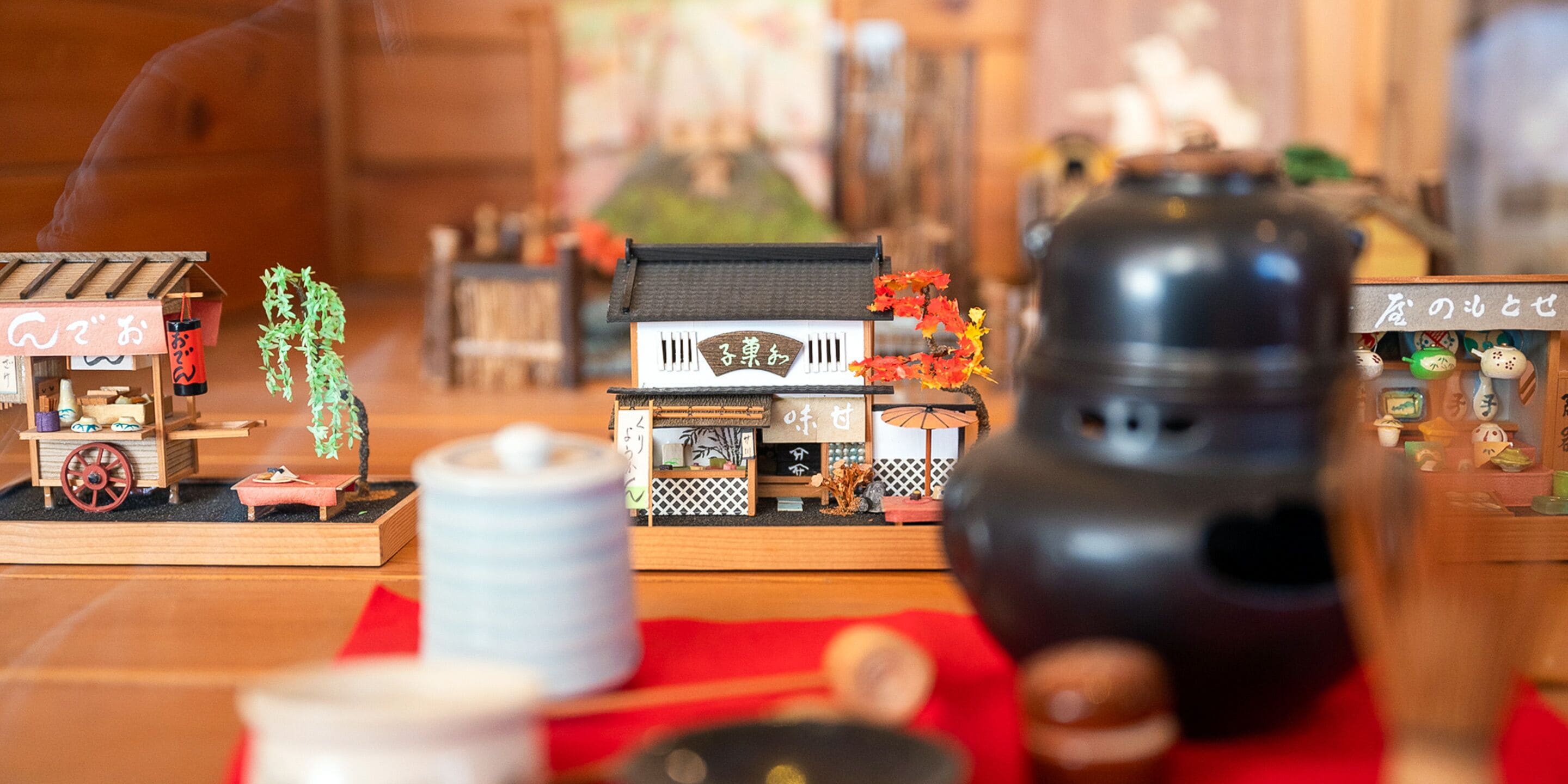Uma miniatura de uma aldeia tradicional japonesa, com casas de madeira, um bule de chá e uma pequena loja.