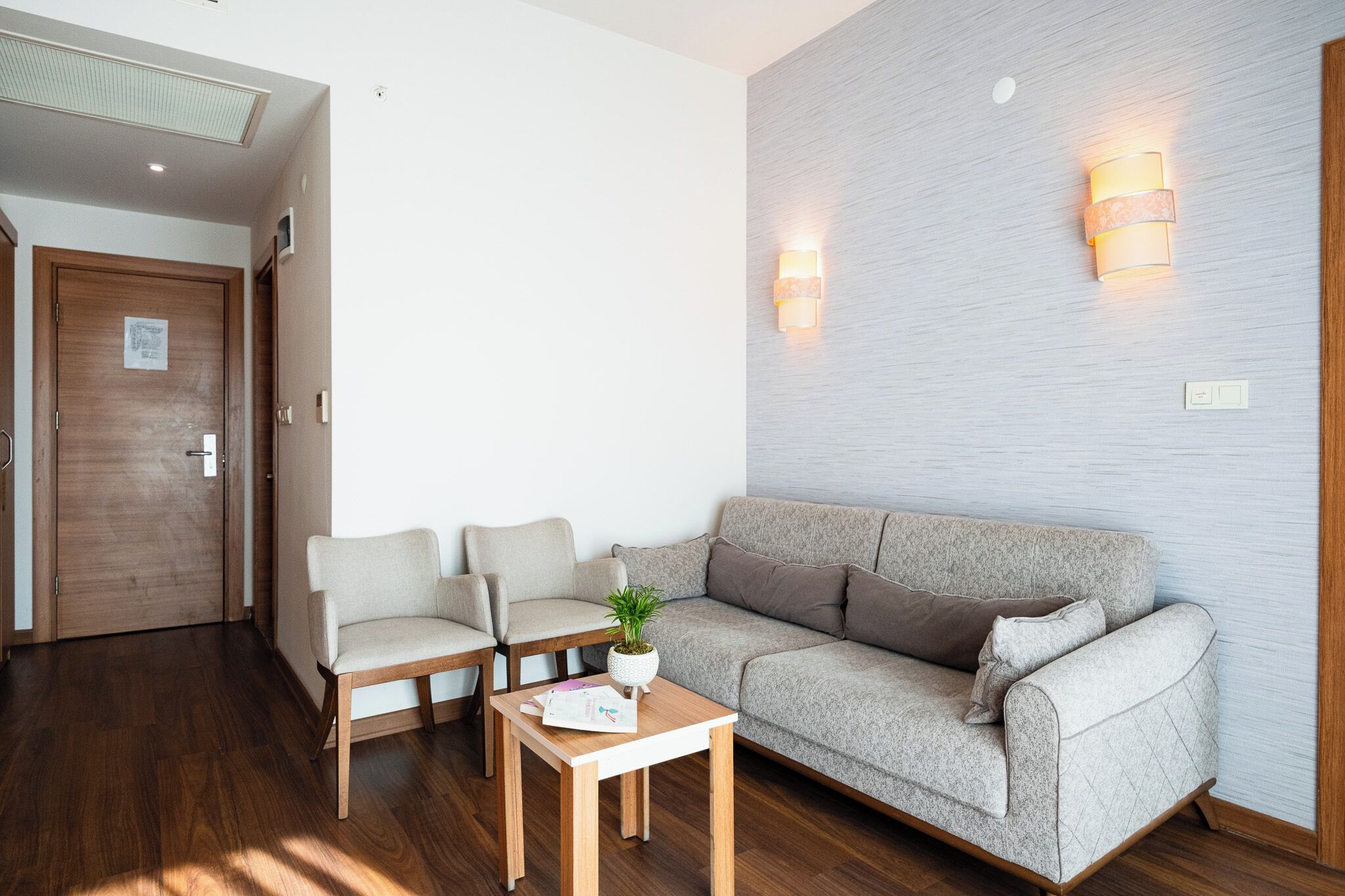 Uma sala de estar moderna com um sofá cinzento, duas poltronas, uma mesa de centro de madeira e uma pequena planta em vaso.