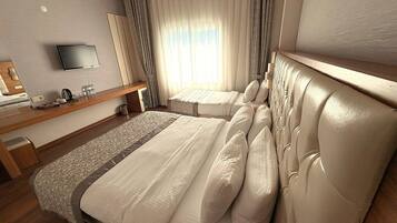 Quarto de hotel com duas camas, televisão, escrivaninha com artigos de higiene e janela com cortinas.