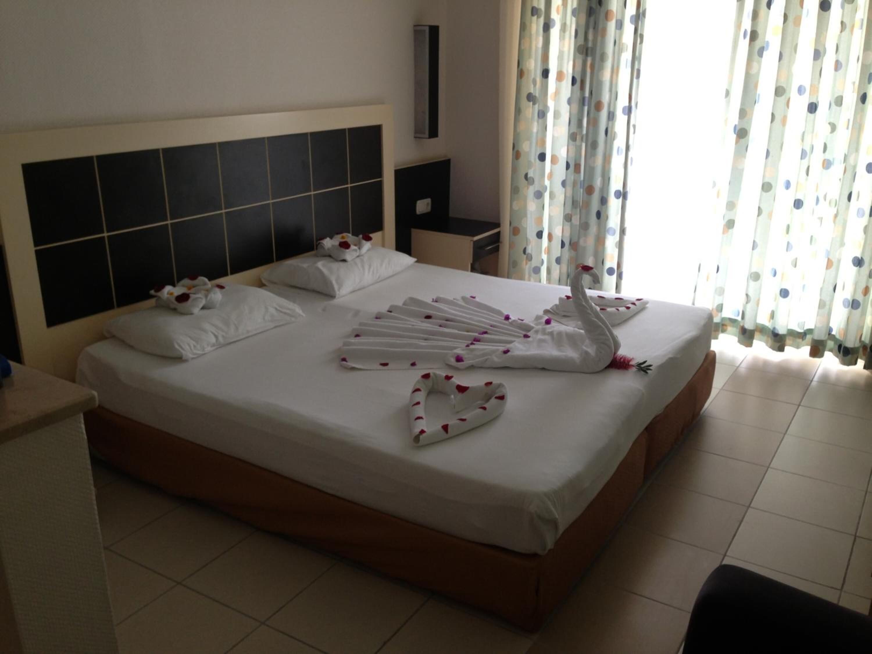Quarto de hotel com cama bem arrumada, cabeceira, mesa de cabeceira e janela com cortinas.