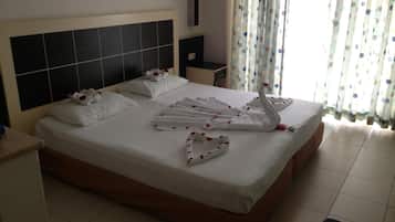 Quarto de hotel com cama bem arrumada, cabeceira, mesa de cabeceira e janela com cortinas.