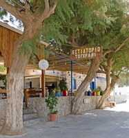 Uma área de estar rústica ao ar livre, com um pérgola de madeira, plantas em vasos e uma placa com a inscrição 'ΕΣΤΙΑΤΟΡΙ ΤΟΡΕΠΑΝΙ'.