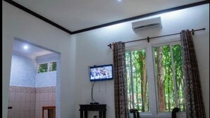 Quarto de hotel com uma cama, televisão fixada na parede, janela com cortinas e ar condicionado.