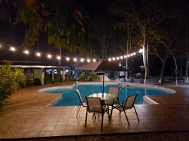 Área de piscina ao ar livre com mesa e cadeiras, cercada por um pátio ladrilhado.