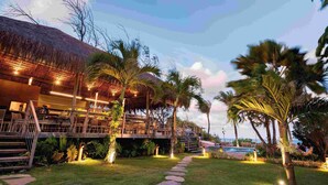 Resort com estrutura de colmo, piscina e caminho de pedra que leva ao edifício.