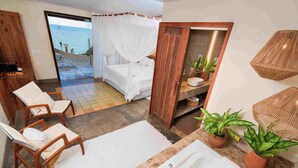 Quarto com cama grande, espaço de estar com cadeiras, banheira e vista para o mar.