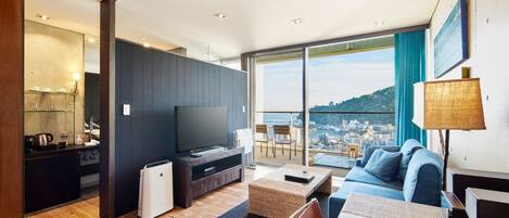 Uma sala de estar moderna com uma televisão grande, um sofá, uma mesa de jantar e uma varanda com vista para a cidade.