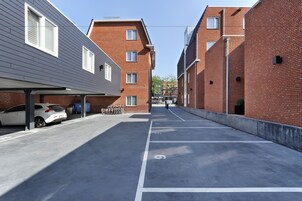 Uma área de estacionamento com vagas demarcadas, um carro branco e um edifício com paredes de tijolo e janelas.