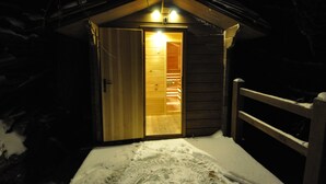 Uma cabana de madeira com interior iluminado, uma porta de madeira e chão coberto de neve.