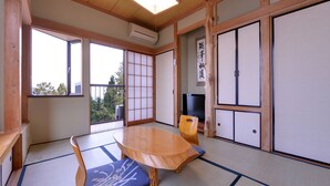 Um quarto japonês tradicional, com tatames, uma mesa de madeira baixa, portas deslizantes e uma televisão.