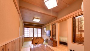 Um quarto tradicional japonês com piso de tatame, uma mesa de madeira baixa, uma televisão e uma porta corrediça com um painel decorativo.