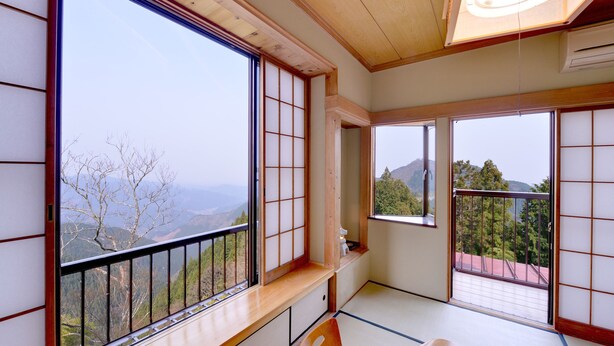 Um quarto japonês tradicional com piso de tatame, portas deslizantes e amplas janelas com vista para as montanhas.