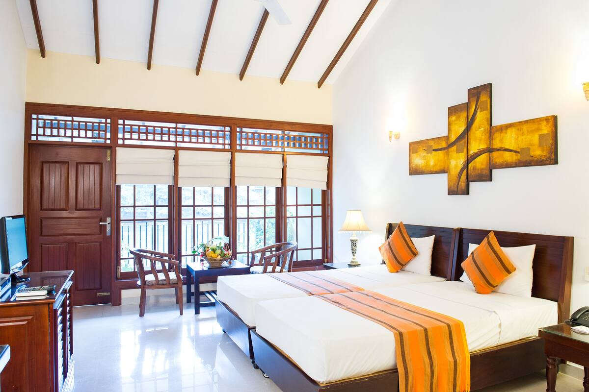 Quarto de hotel com uma cama grande, uma escrivaninha com computador, uma cadeira e uma janela com vista.