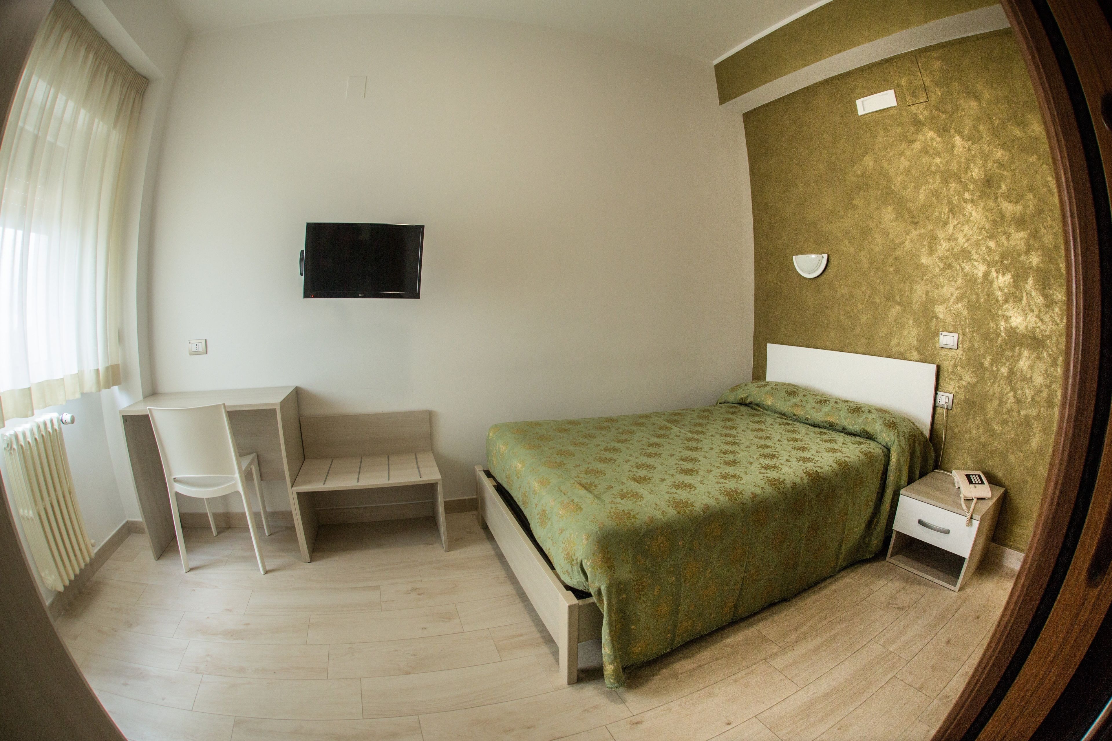 Quarto com cama, escrivaninha, cadeira, televisão e mesa de cabeceira.