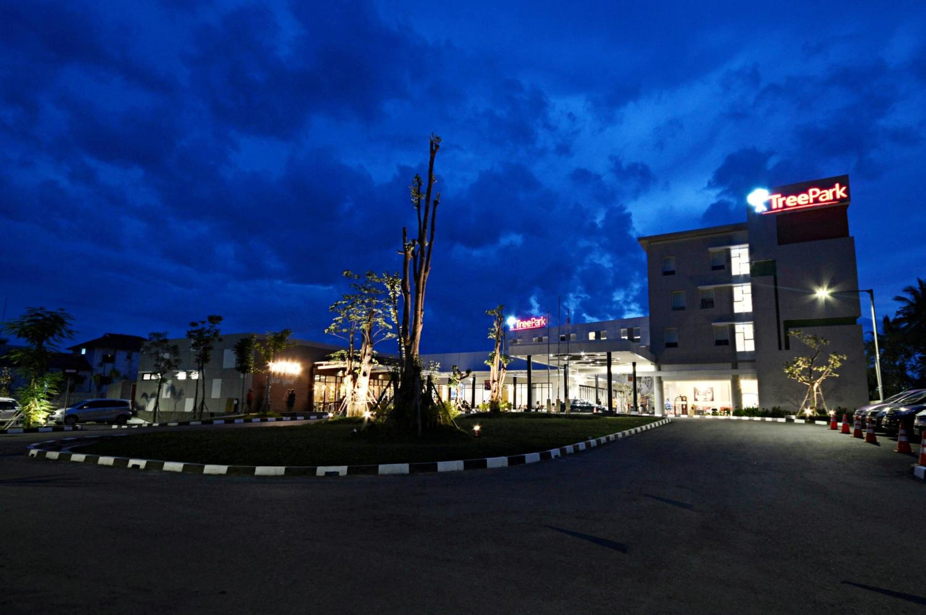 Um hotel TreePark com design moderno, apresentando uma placa de destaque, área de estacionamento e um jardim ajardinado.