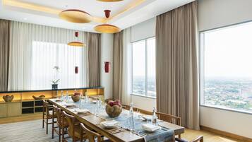 Uma sala de jantar com uma mesa comprida posta para seis pessoas, janelas amplas com cortinas e luminárias pendentes.