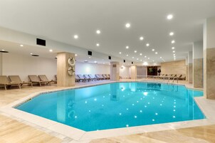 Piscina interna com piso azulejado, espreguiçadeiras e iluminação embutida no teto.