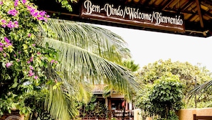 Entrada de um jardim tropical com uma placa indicando 'Bem-Vindo/Welcome/Bienvenido'.
