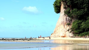 Uma praia com um penhasco imponente e uma faixa de areia.