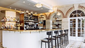 Uma área de bar com balcão, prateleiras de garrafas e banquetas.