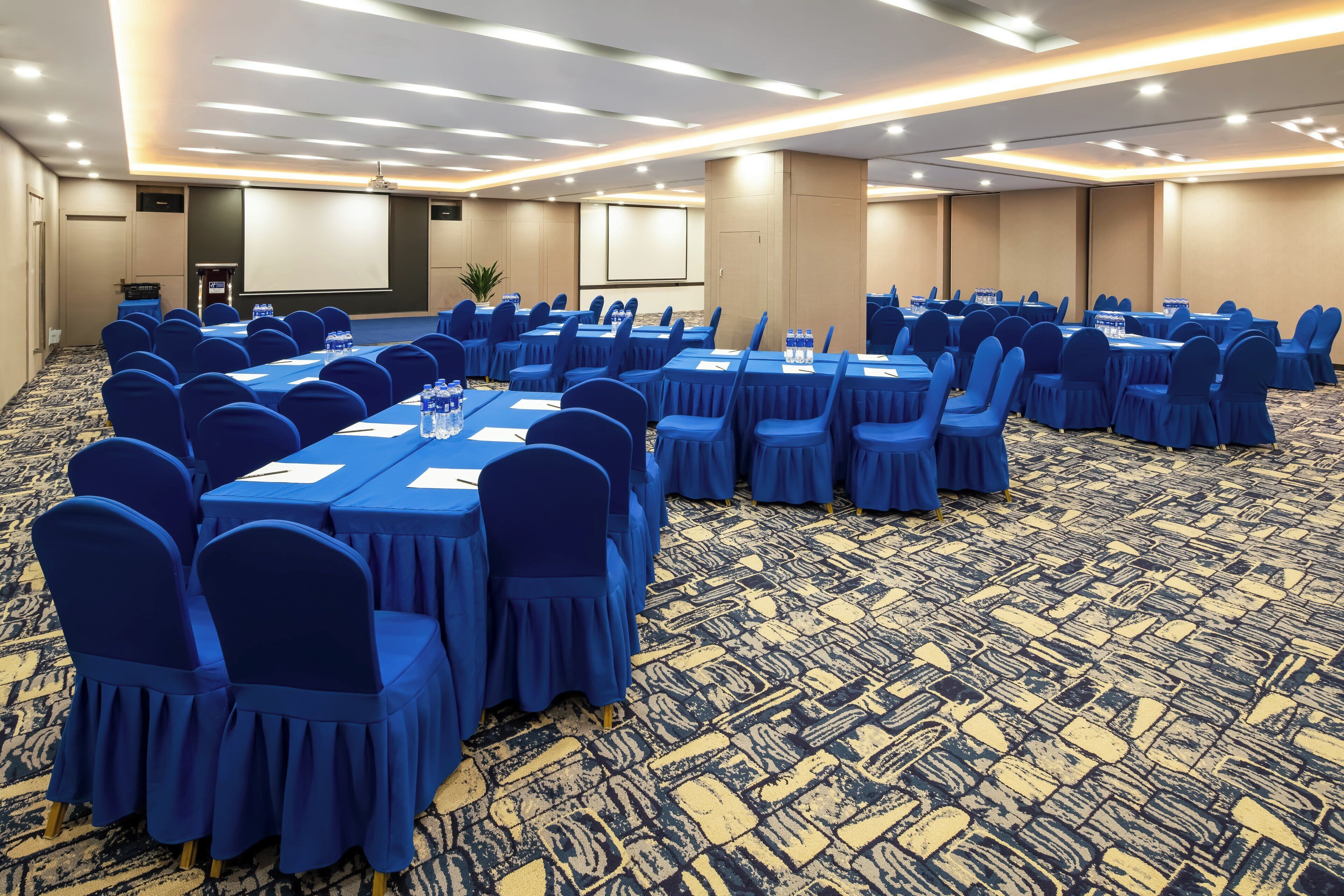 Sala de conferência com várias mesas e cadeiras, equipada com garrafas de água e cartões de identificação.