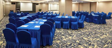 Sala de conferência com várias mesas e cadeiras, equipada com garrafas de água e cartões de identificação.