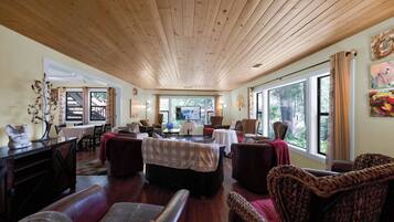 Uma sala de estar ampla com teto de madeira, assentos confortáveis, uma mesa de jantar e grandes janelas com vista para o exterior.