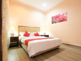 Quarto de hotel com uma cama, duas mesas de cabeceira, um abajur, cortina e um quadro floral na parede.