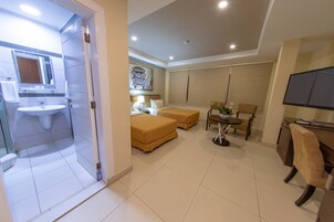 Quarto de hotel com banheiro, cama, escrivaninha e televisão.
