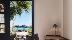Quarto com vista para a praia, uma mesa, uma cadeira e um abajur.