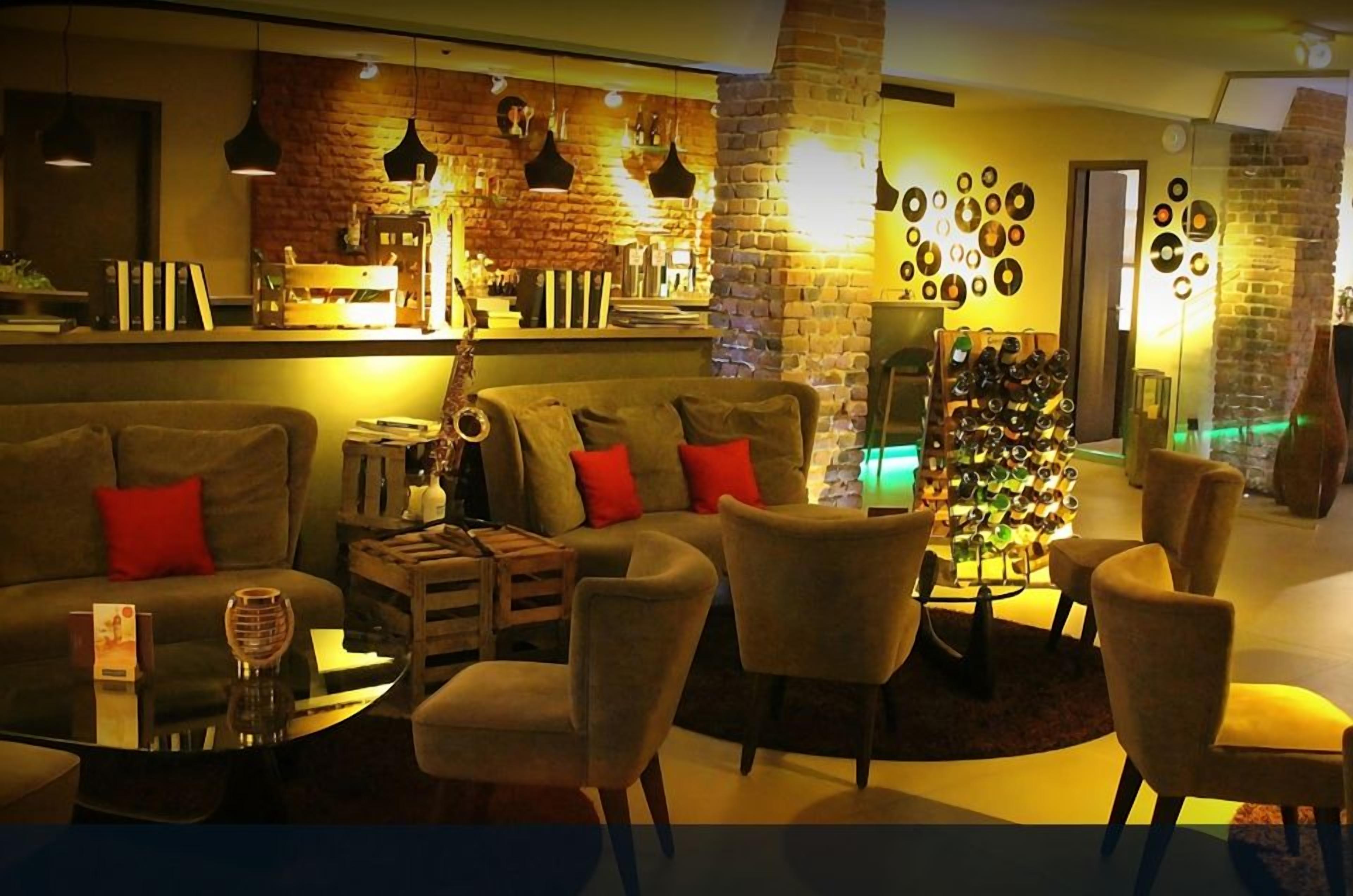 Uma área de estar acolhedora com sofás e poltronas, uma mesa de centro e um espaço para vinhos. É visível o texto 'Frühstück & Parkplatz inklusive'.