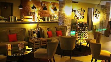 Uma área de estar acolhedora com sofás e poltronas, uma mesa de centro e um espaço para vinhos. É visível o texto 'Frühstück & Parkplatz inklusive'.