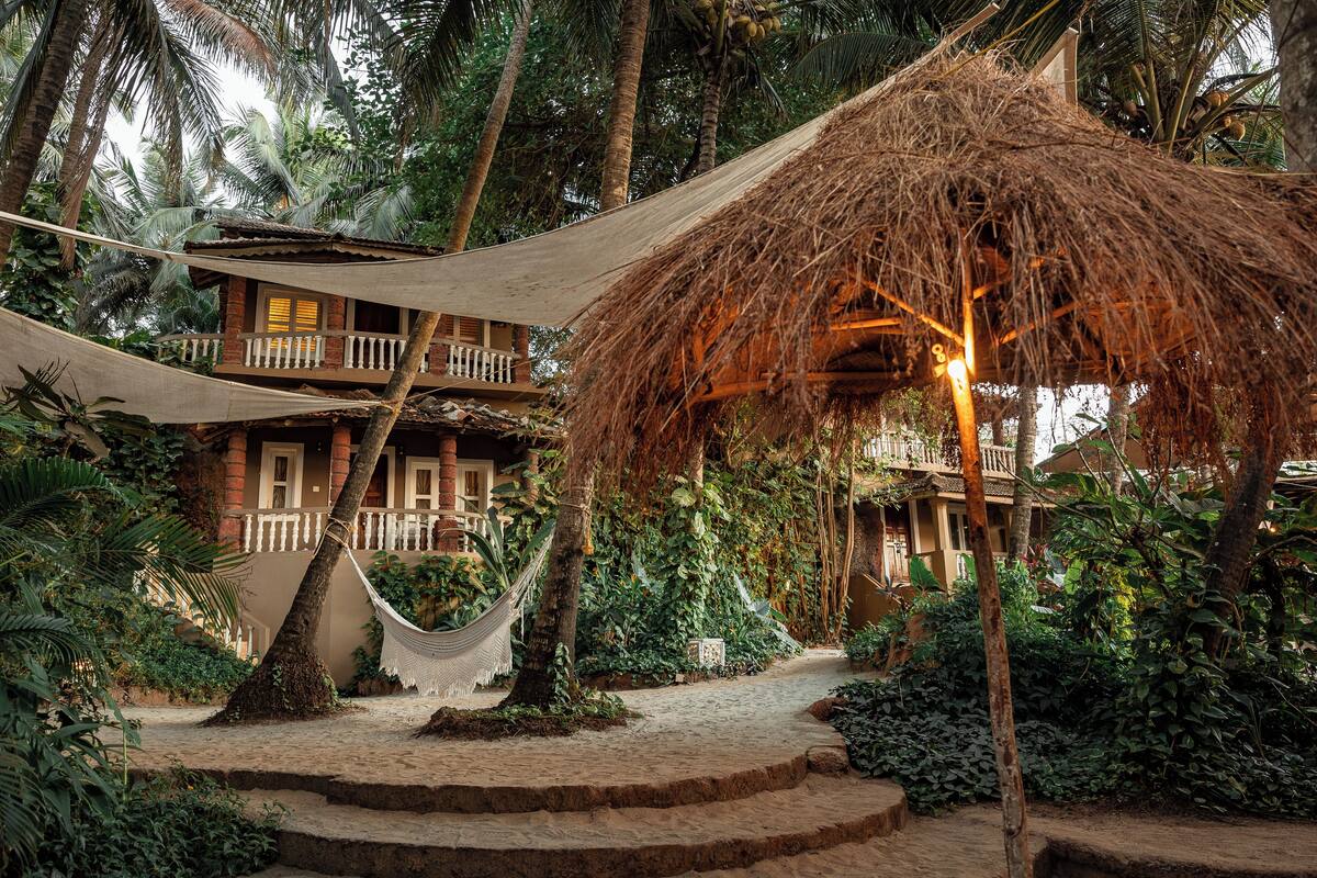 Um resort tropical com uma rede, estruturas com telhado de palha e vegetação exuberante.
